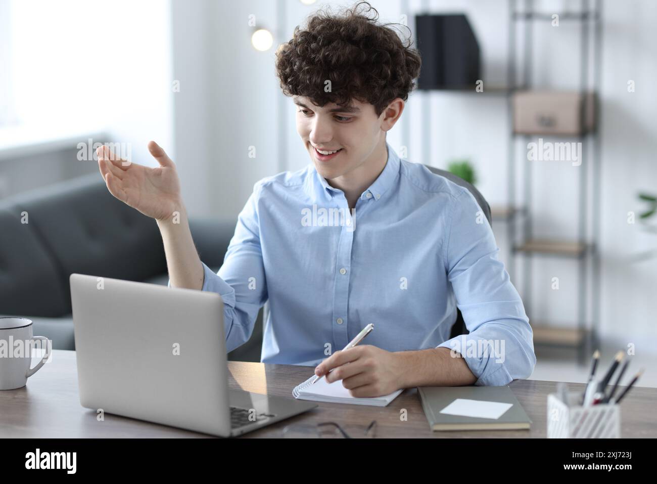 Teenager taking notes while working with laptop at table indoors ...