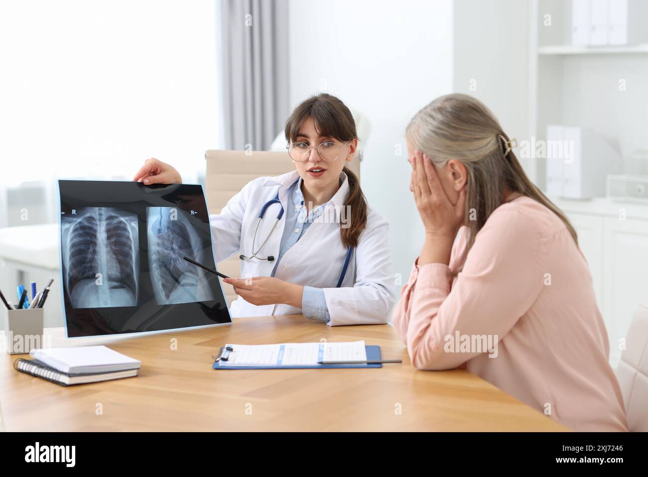 Lung disease. Doctor showing chest x-ray to her patient at table in ...
