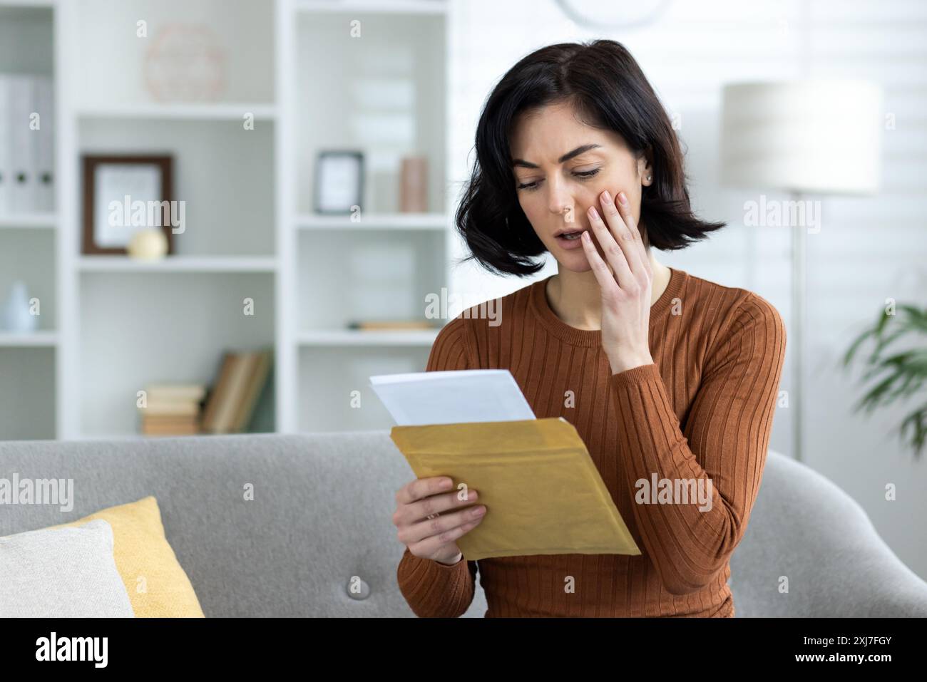 Close-up photo of worried and shocked young woman sitting on sofa at ...