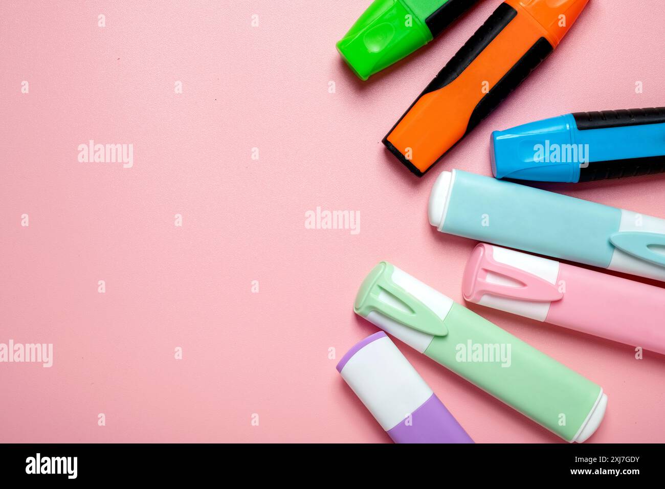 A row of markers of various colors are on a pink background. The ...