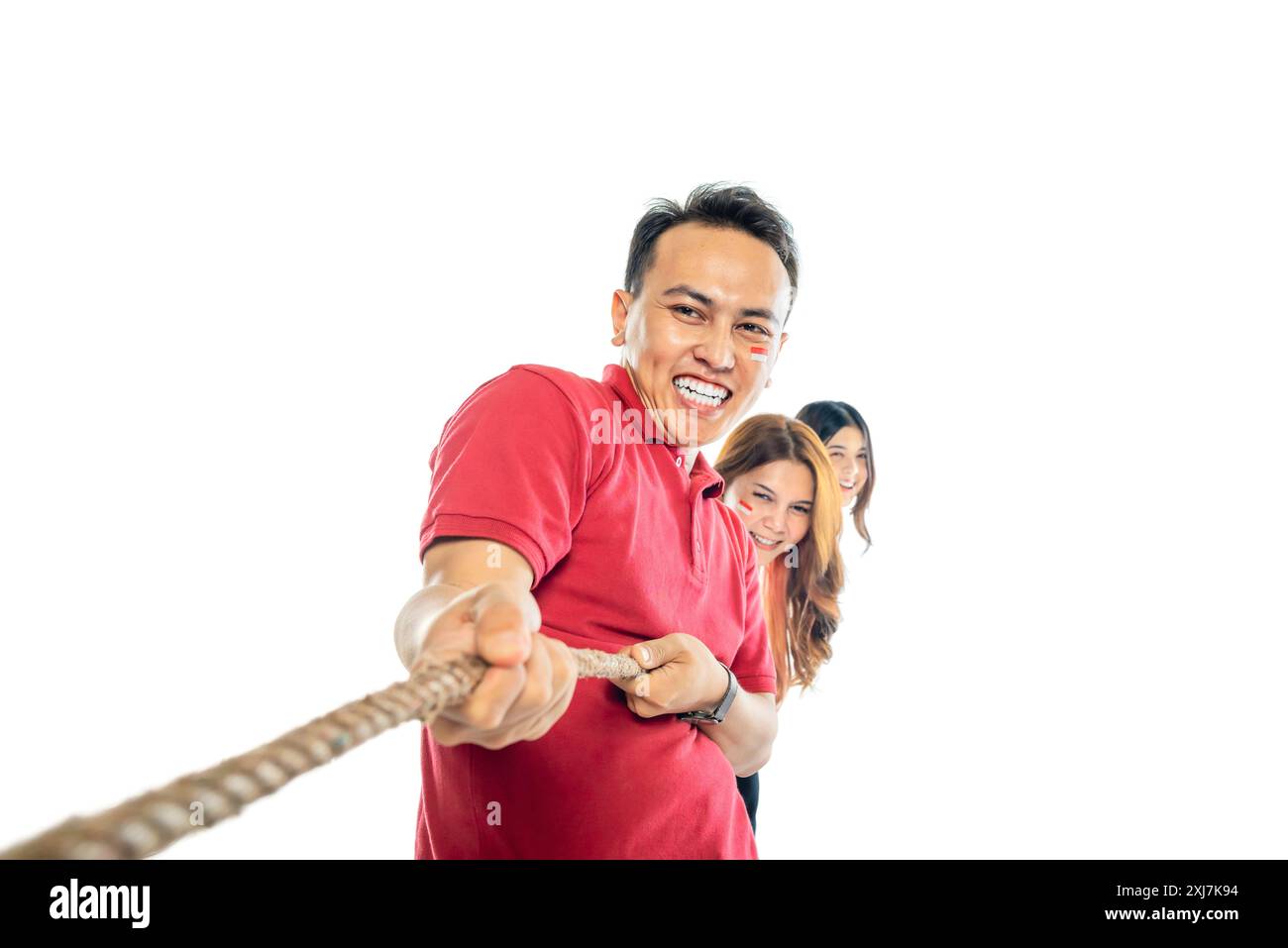 A man in a red shirt is pulling a rope on playing tug of war. The man ...
