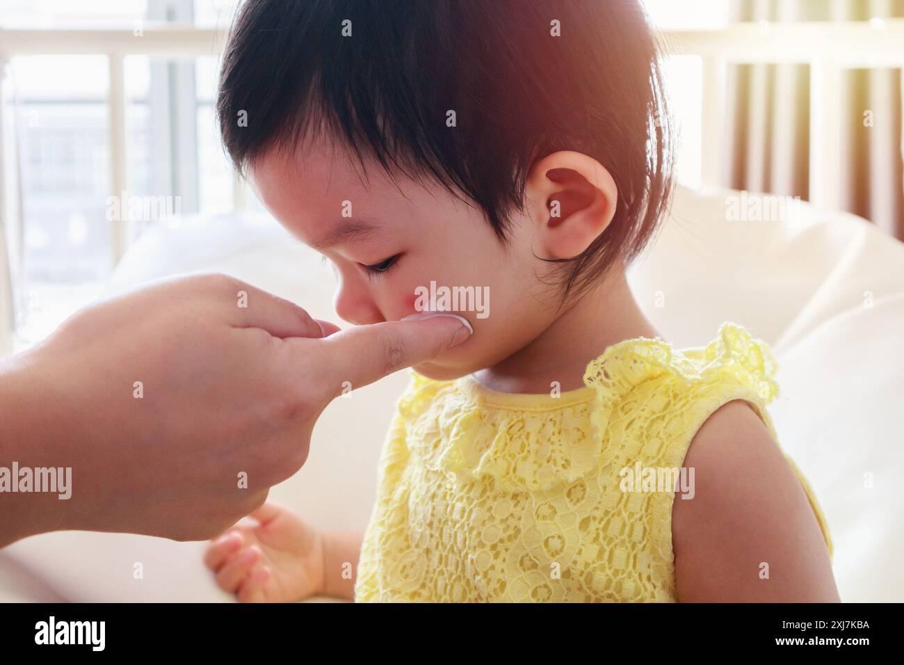 mother applying antiallergic medicine cream at cute asian girl face ...