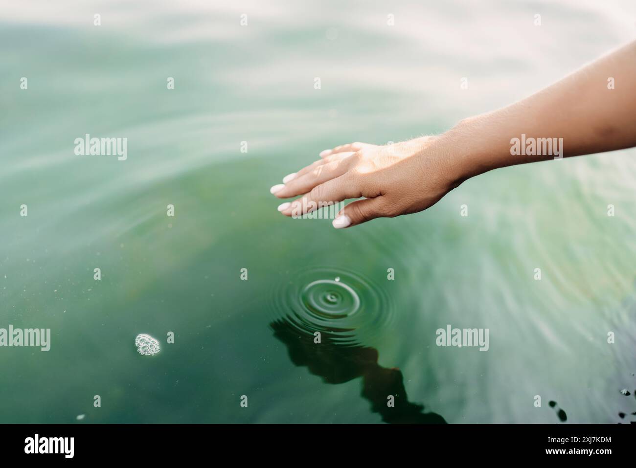 The hand touches the water, creating ripples. The water is calm and ...
