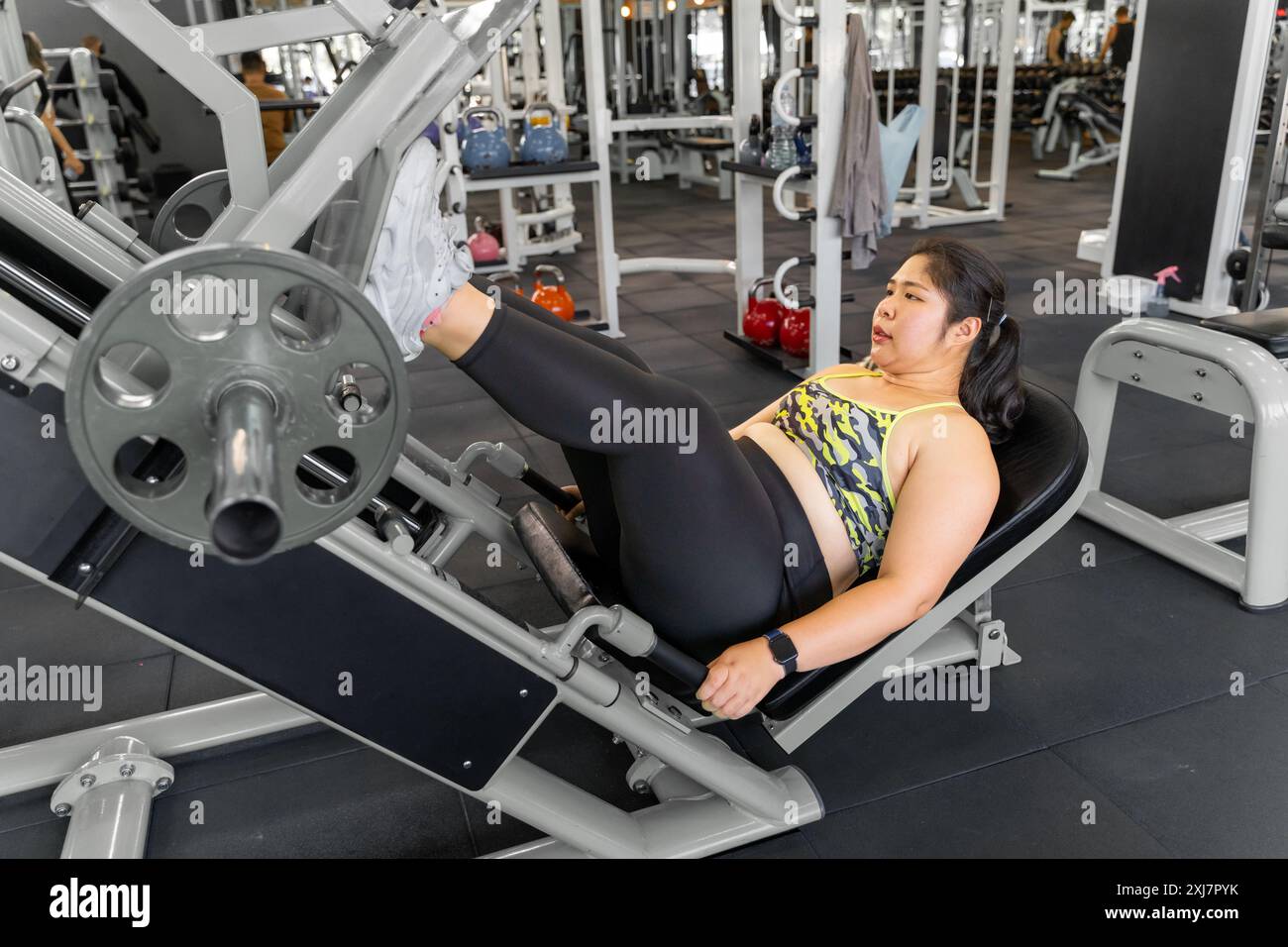Young overweight woman using leg press machine to work on her legs ...