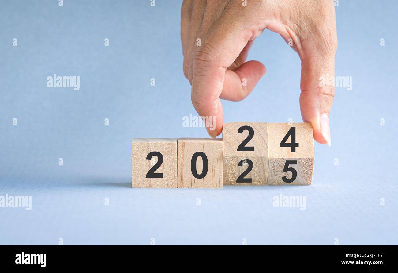 Fingers turning from 2024 to 2025, numbers on wood blocks. On blue ...