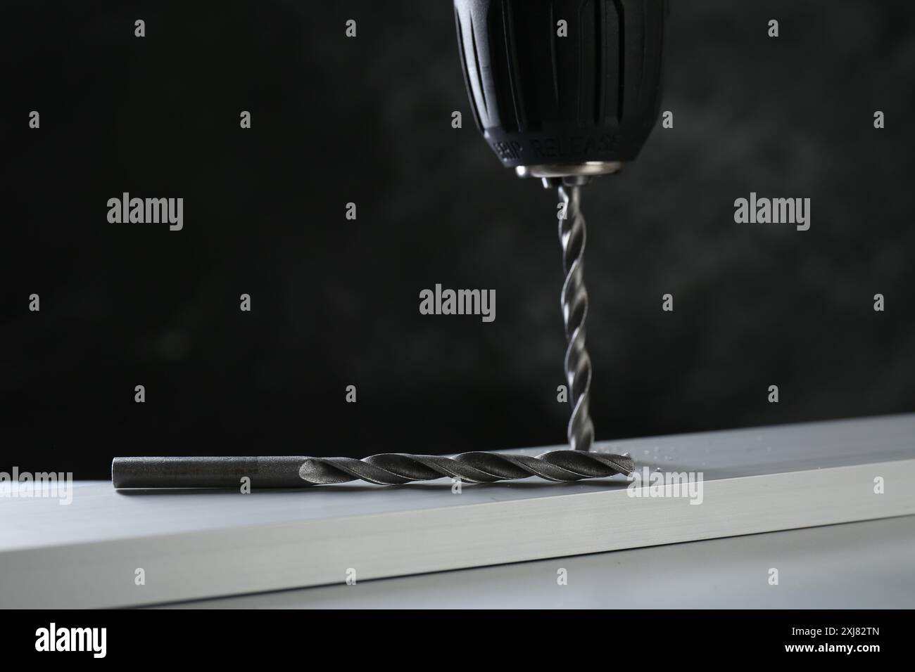 Drilling hole in plank on white table against black background, closeup ...