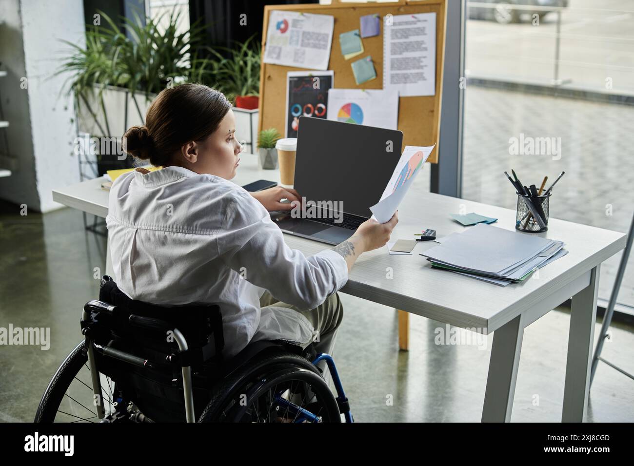 A young businesswoman in a wheelchair works at a modern office desk ...