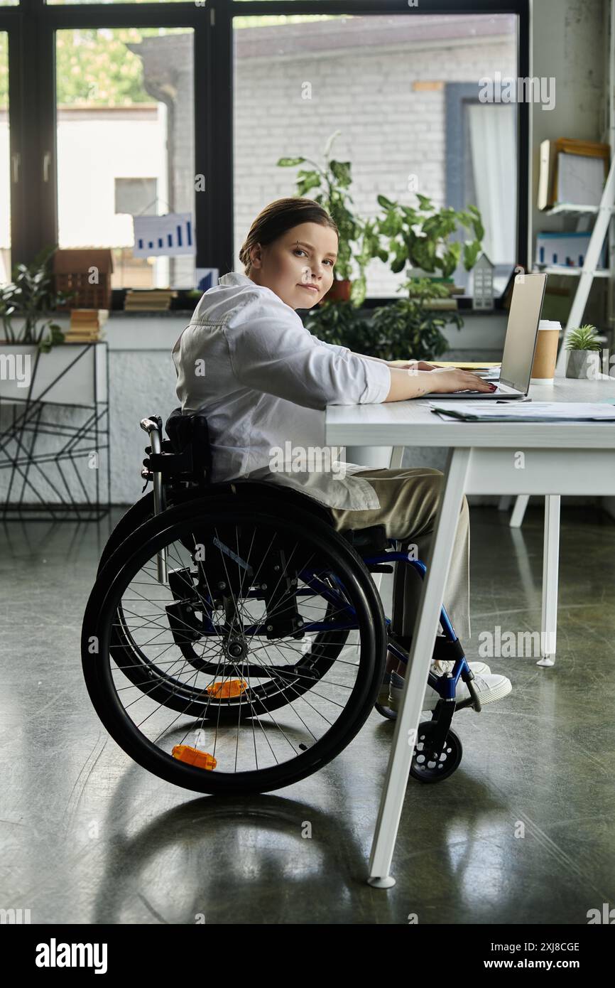A young businesswoman in a wheelchair works at a desk in a modern ...