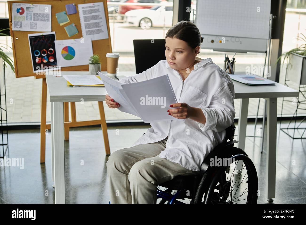 A young businesswoman in a wheelchair sits at a desk in a modern office ...
