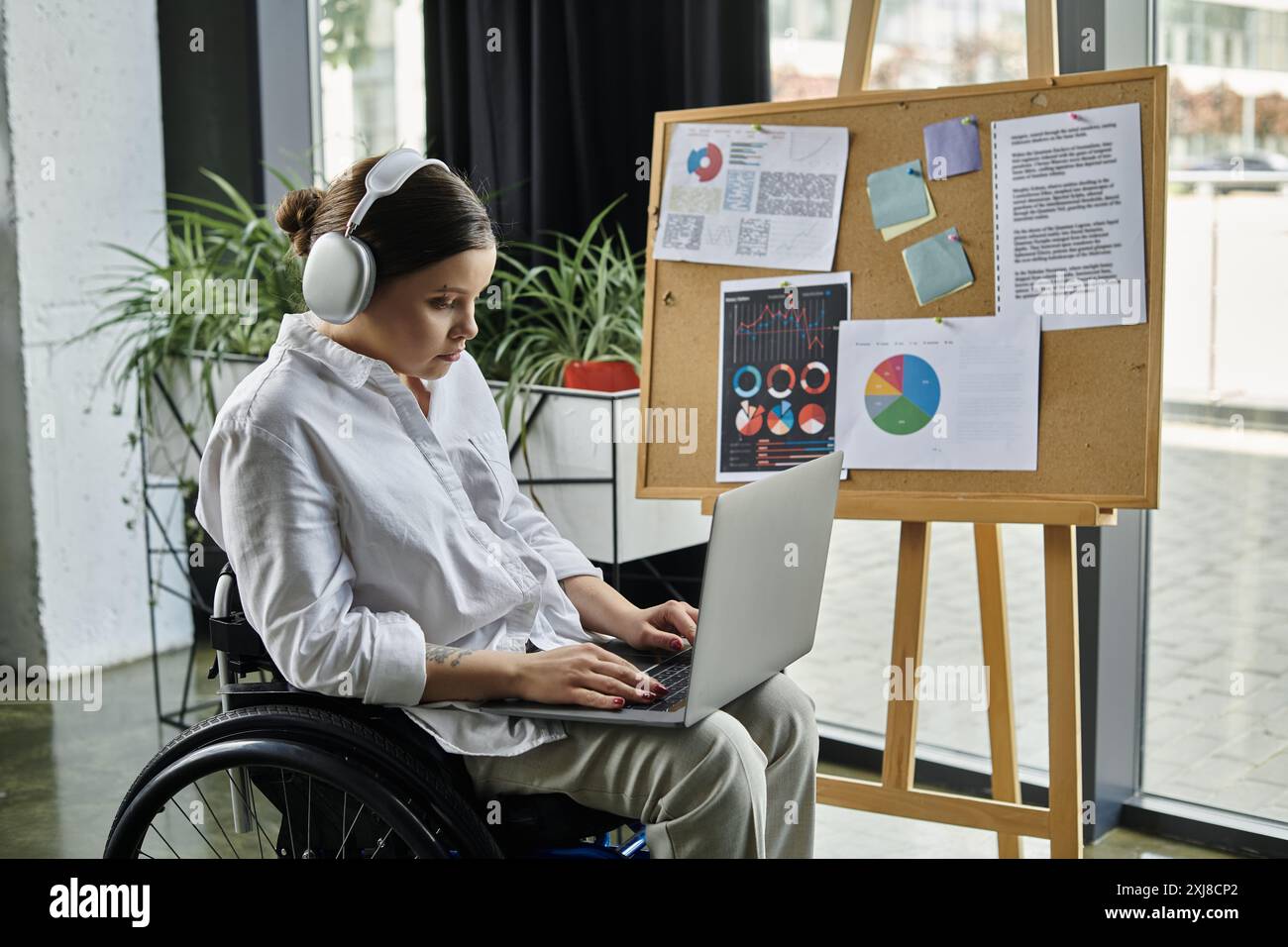 A young businesswoman in a wheelchair works on a laptop in a modern ...