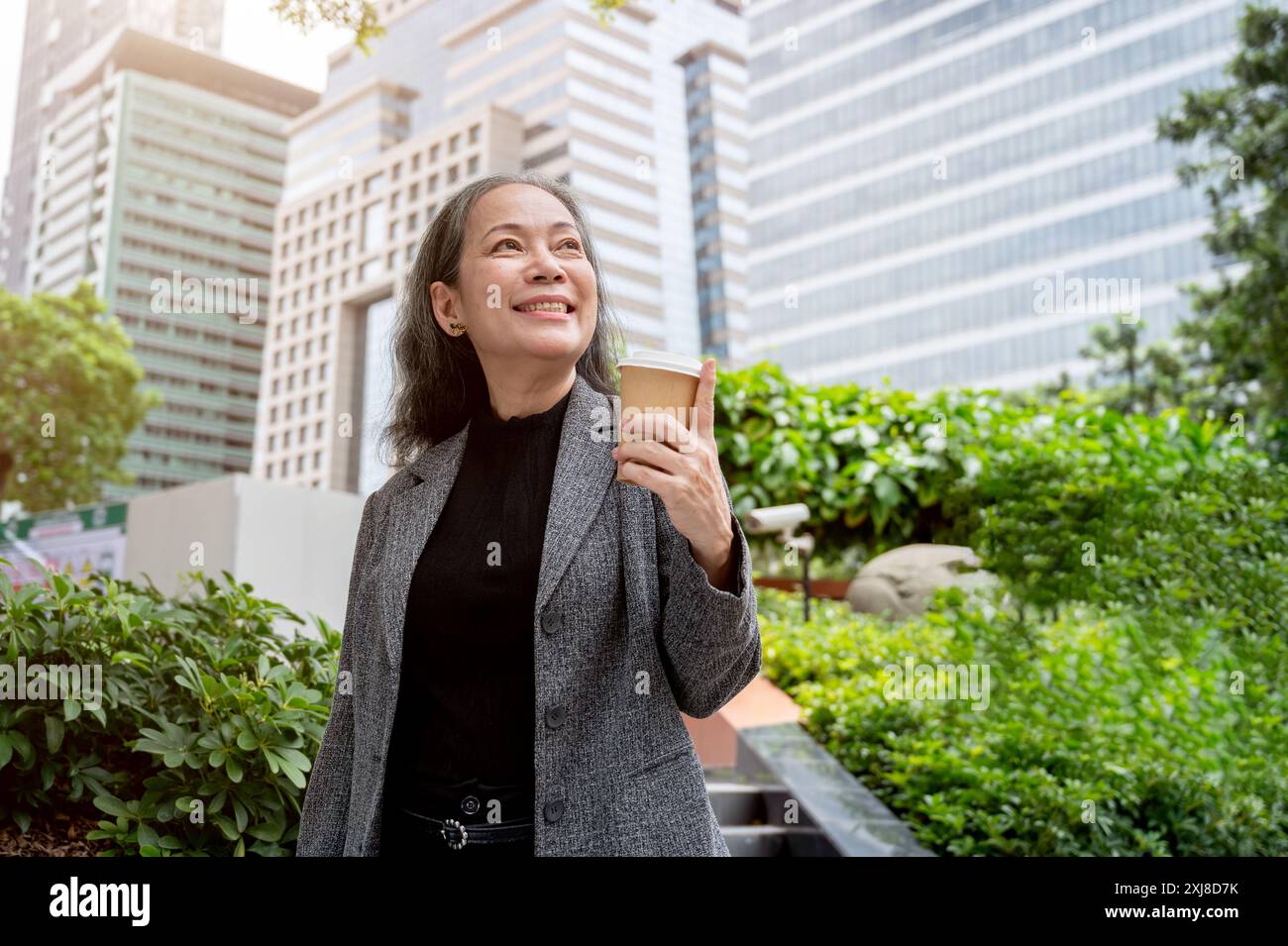 A positive, successful mature Asian businesswoman in a suit is holding a takeaway coffee cup ...
