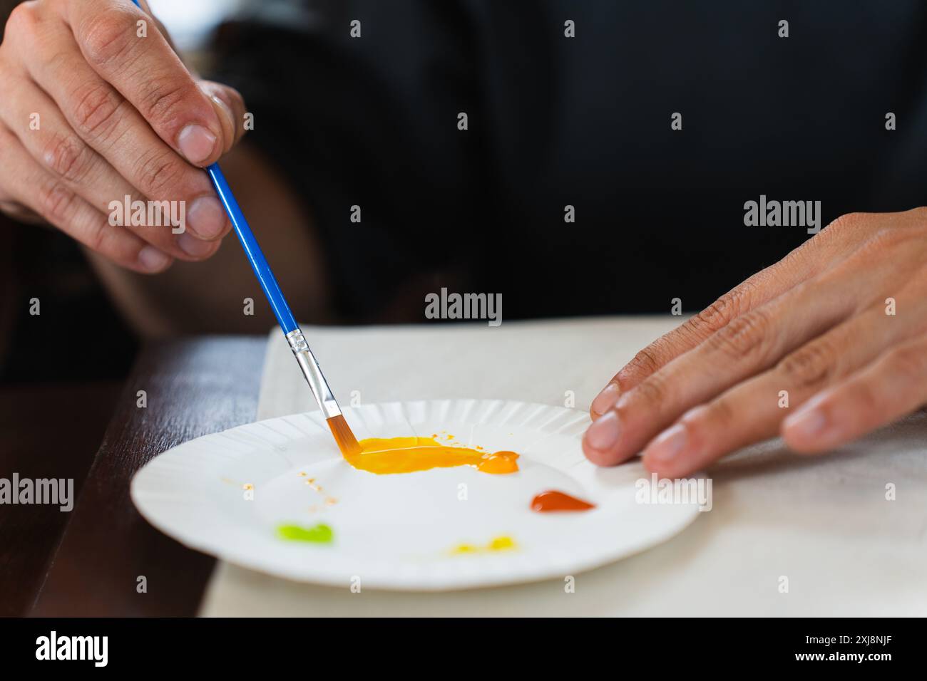 Hands of a man picking up paint with a brush from the color palette ...