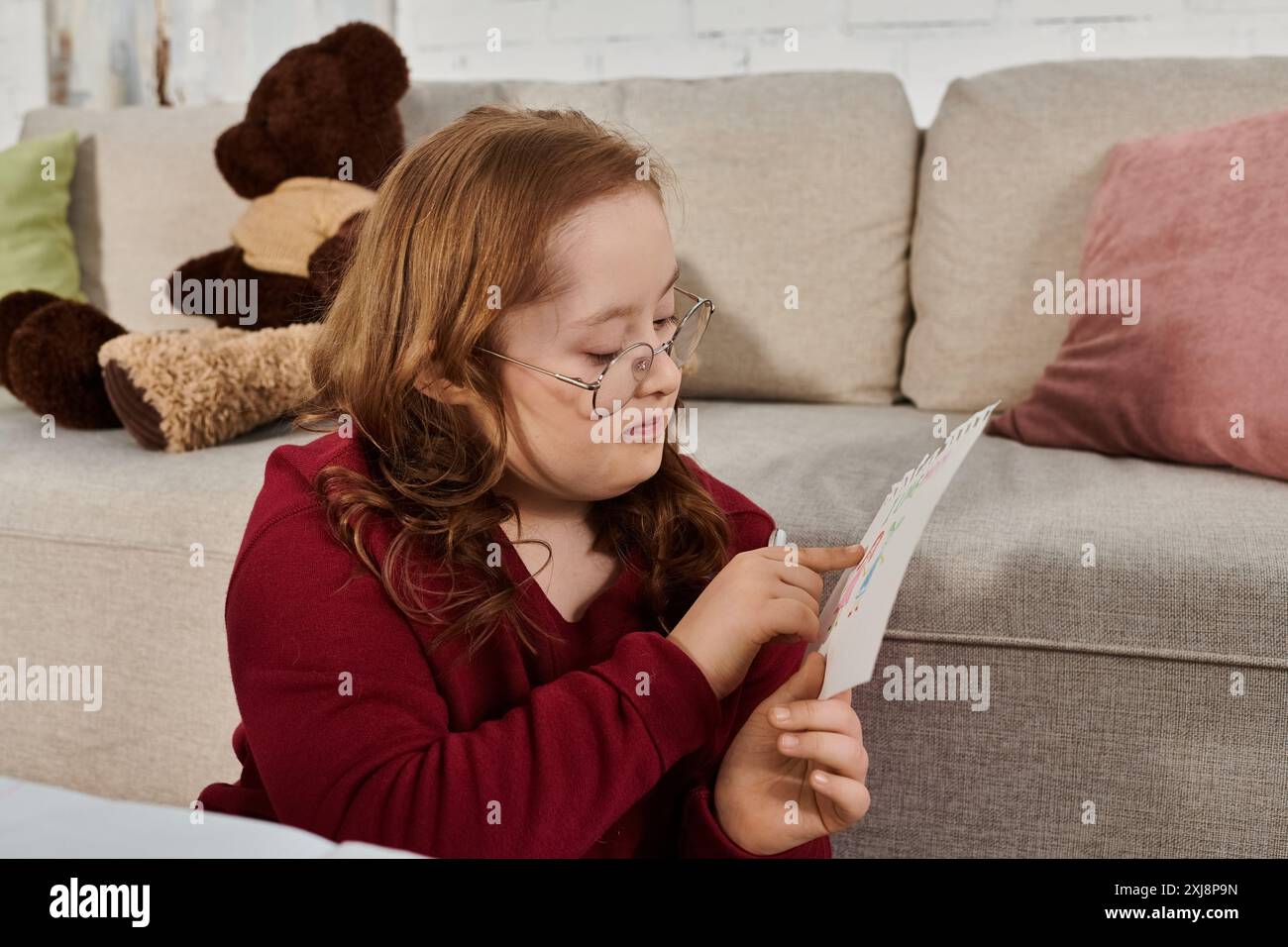 A little girl with Down syndrome sits on the floor, intently studying a ...