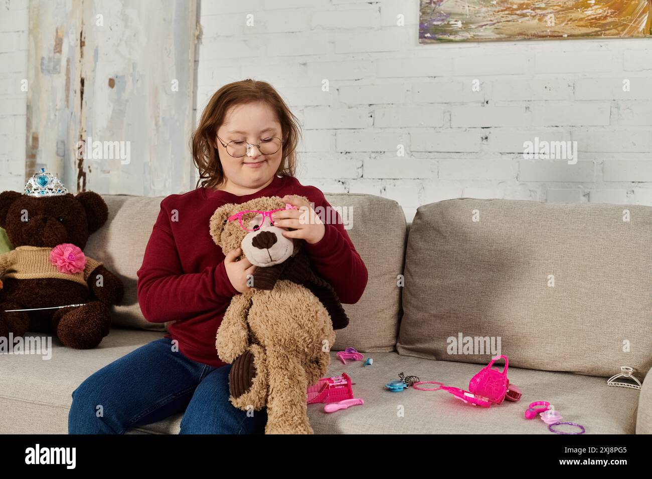 A little girl with Down syndrome plays with a teddy bear in her home ...