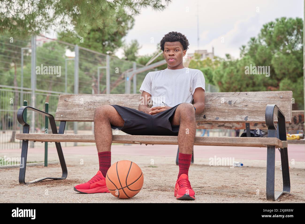 young basketball player waiting sitting on a bench with a ball between ...