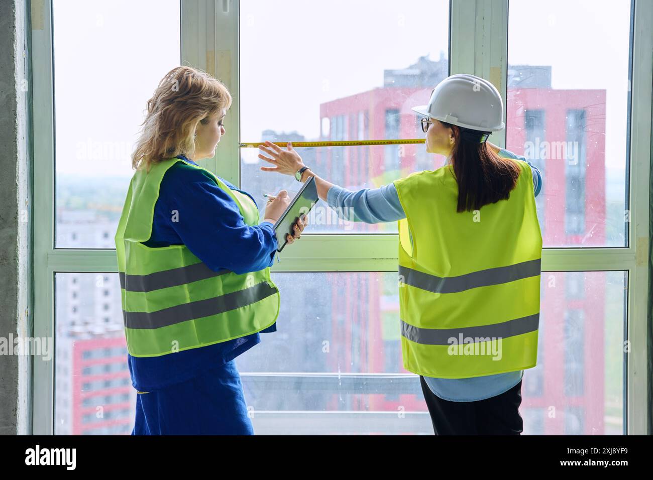 Two female industrial workers taking measurements of windows for ...
