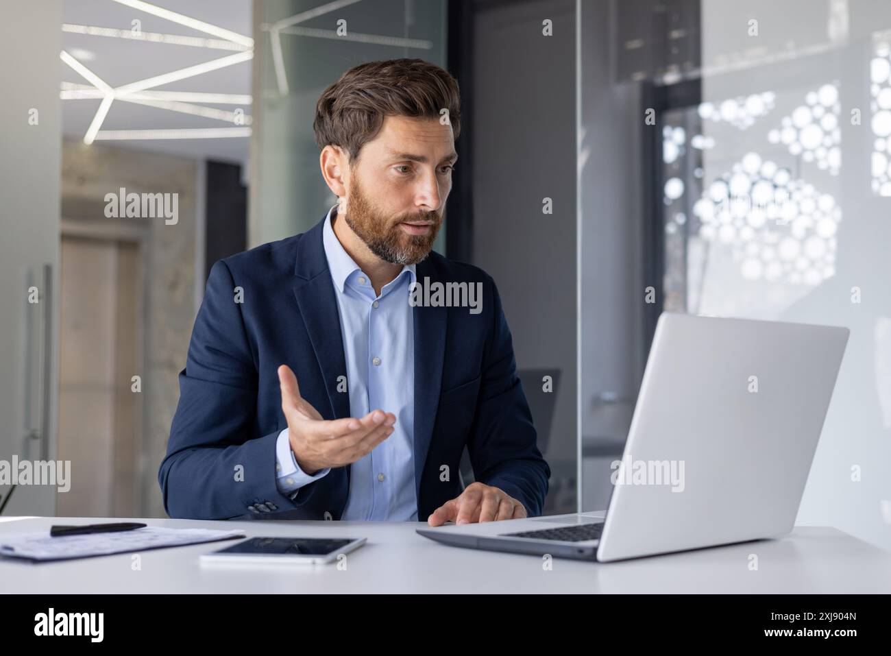 A focused businessman engages in a virtual conversation, articulating ...