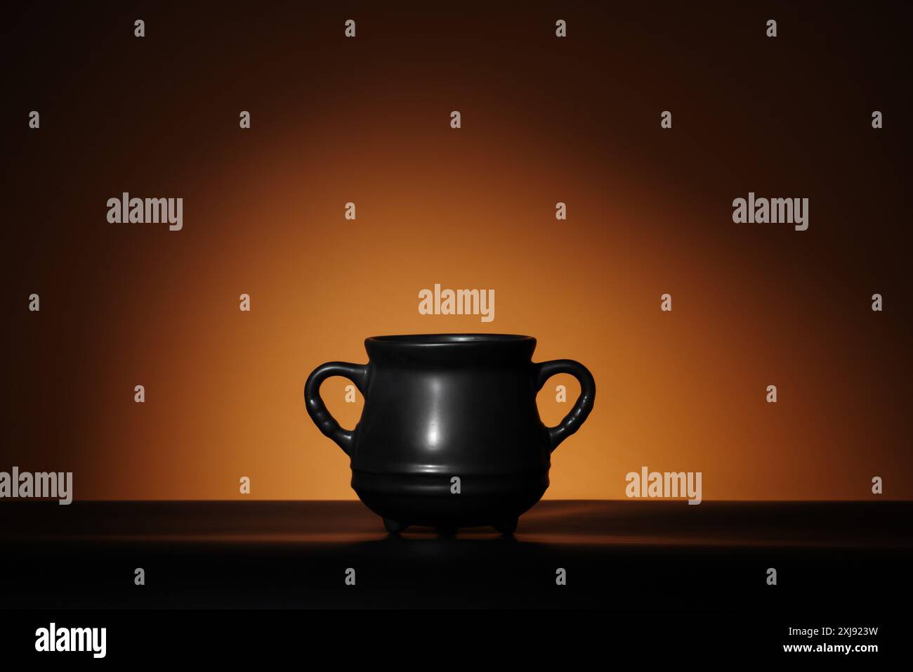 Mysterious black cauldron in spotlight on pumpkin orange background ...