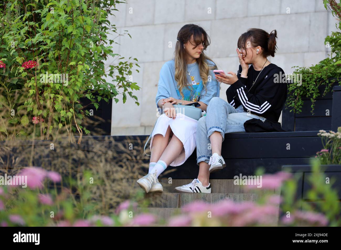 Two girls sitting with smartphone on a bench in city park, emotional ...