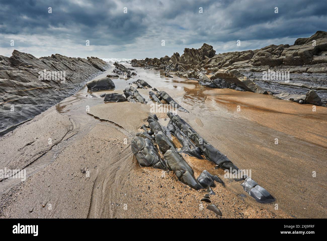 A rocky shore at low tide and under grey skies at Welcombe Mouth ...