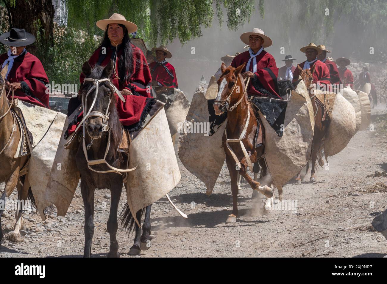 A female gaucho in traditional red Salteño poncho rides at the head of ...