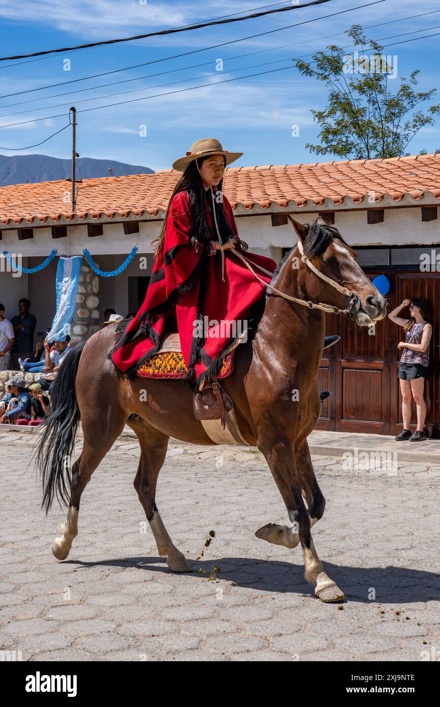 A female gaucho wearing a traditional red Salteño poncho rides ...