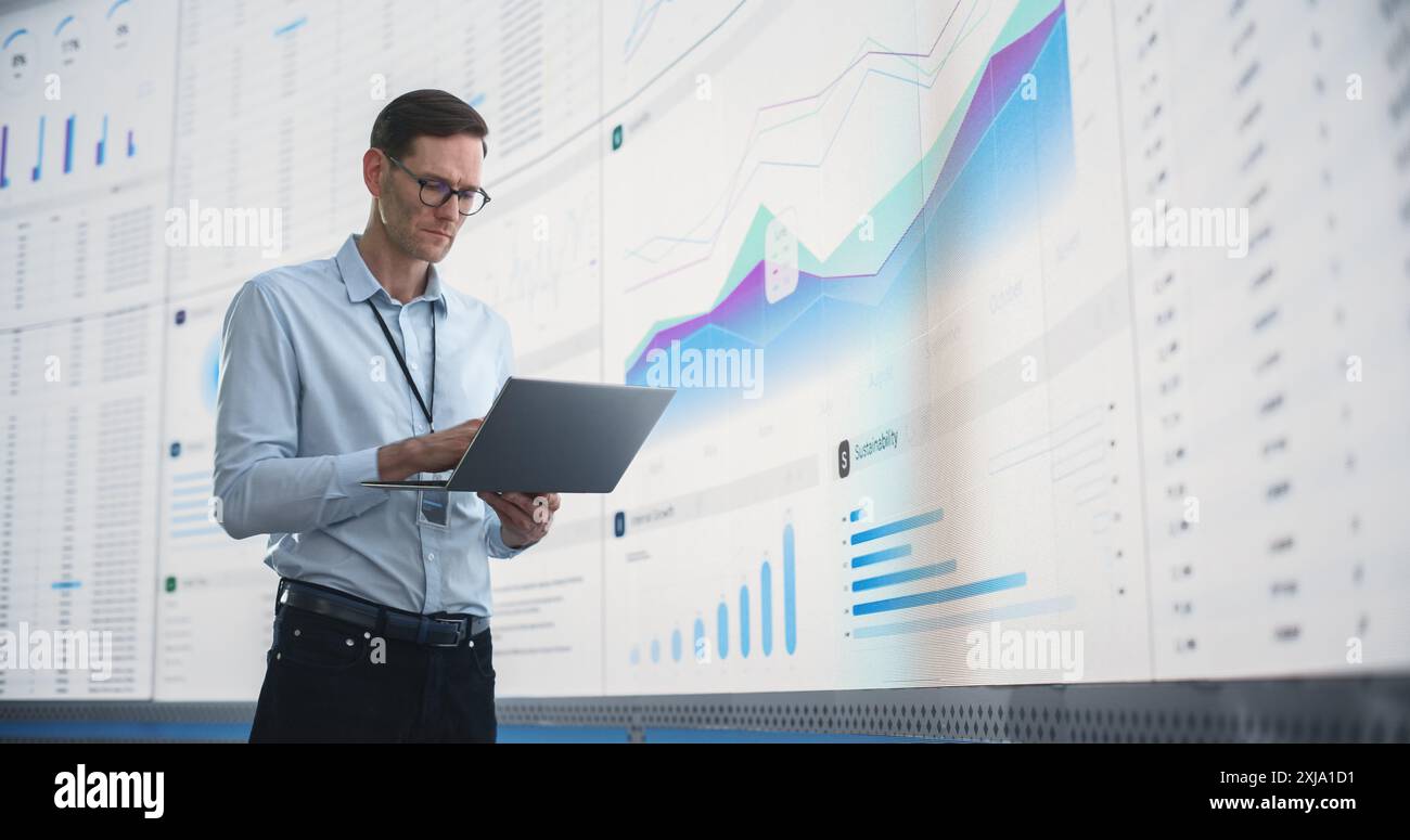 In The Office: Male Monitoring Specialist Holding Laptop Computer And Standing Next To Big ...