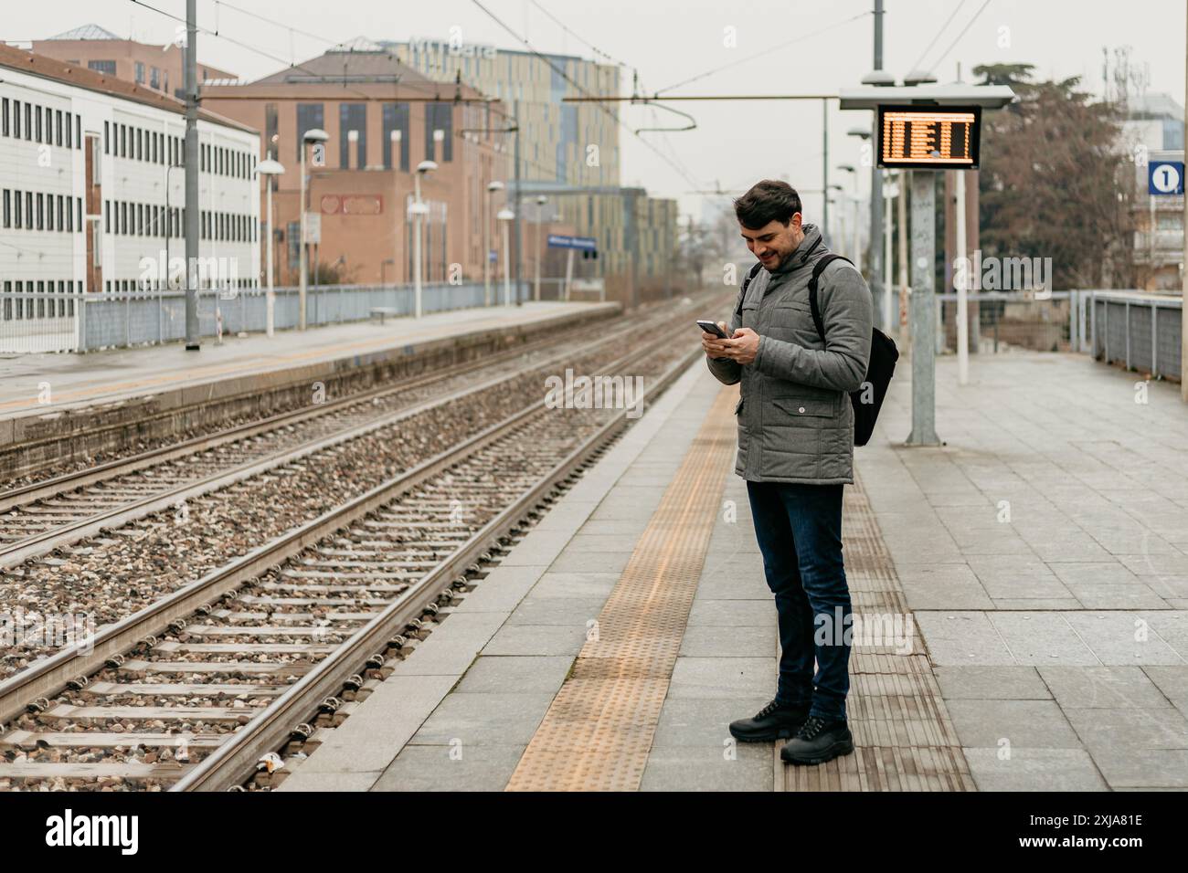 A man stands on a train station platform checking his phone while ...