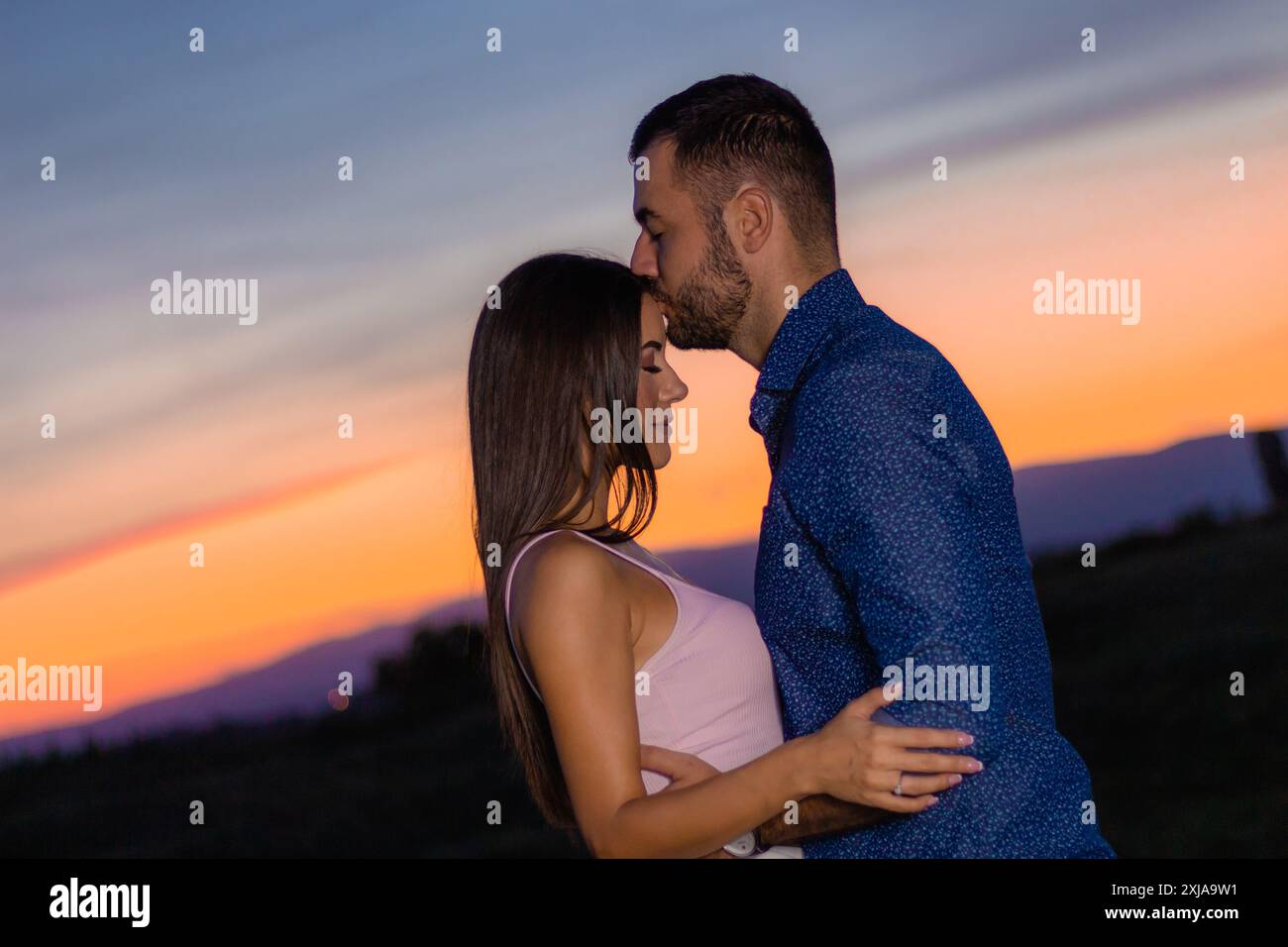 A man in a blue shirt kisses a woman on the forehead while they stand ...