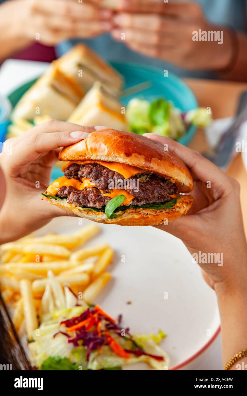 Girl holding a double patty smashed beef burger in a cafe restaurant ...