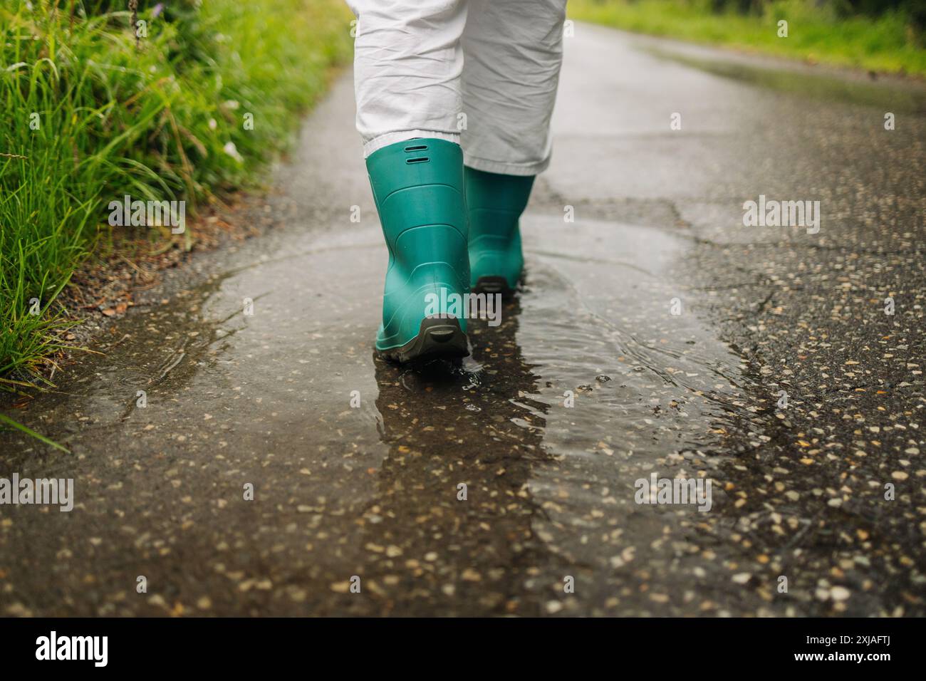 Woman wearing rain rubber boots walking running and jumping into puddle with water splash and ...