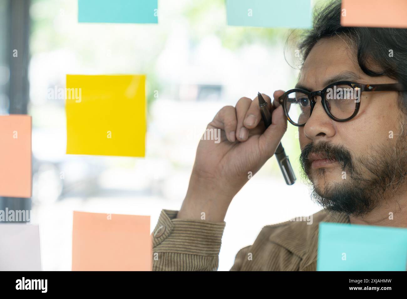 A young man is thoughtfully writing ideas on sticky notes at the office ...