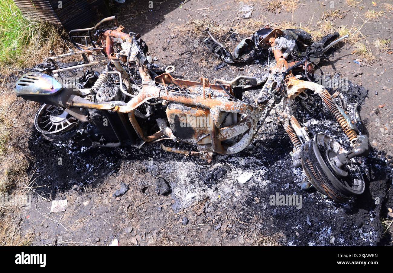 Burnt out motorbike lying on the ground with dark ashes debris in ...