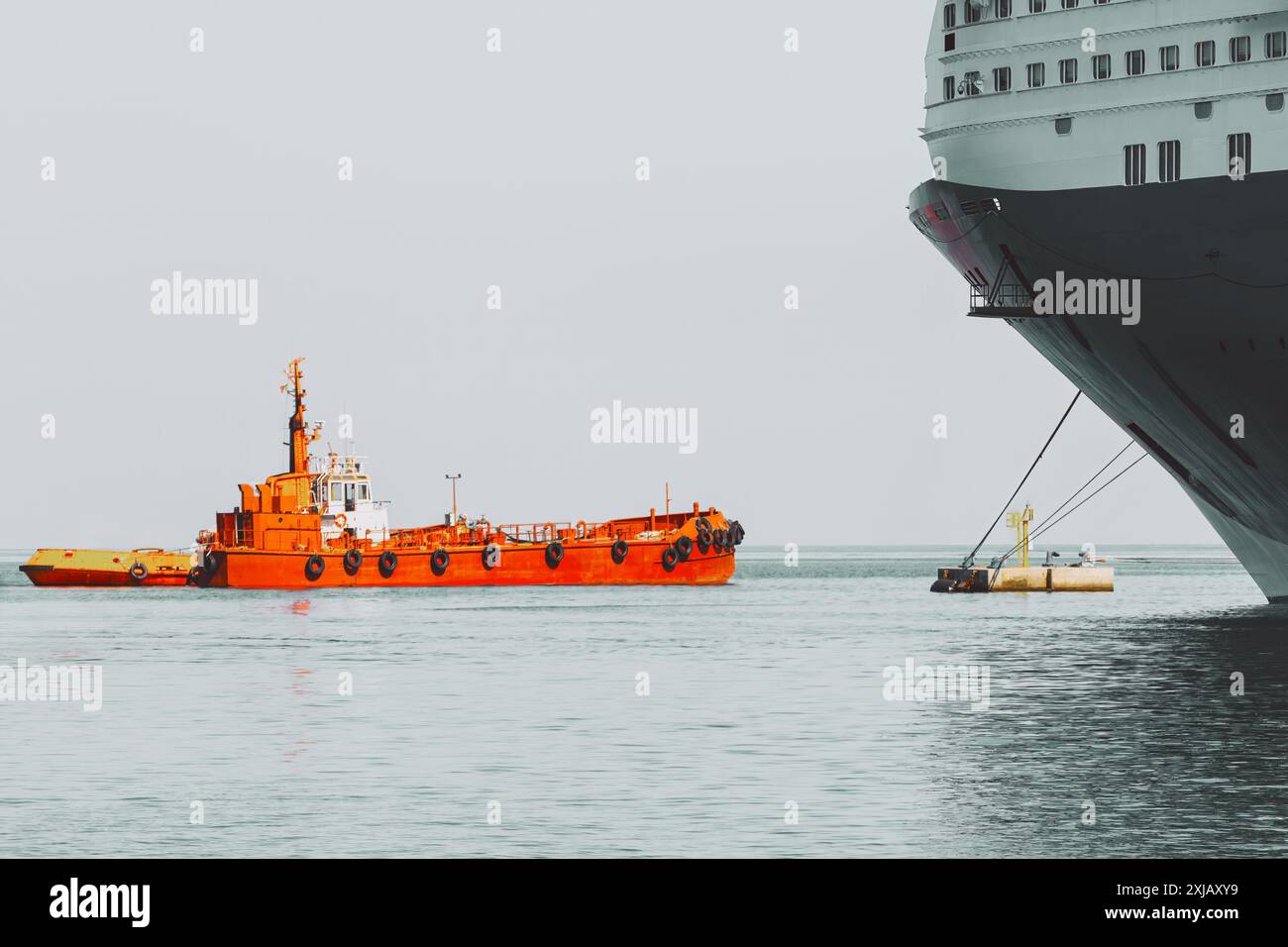 Large ship and a small boat floating in the water. Tugboat is towing ...