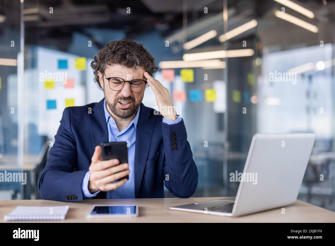 Stressed businessman holding phone with frustrated expression in modern ...