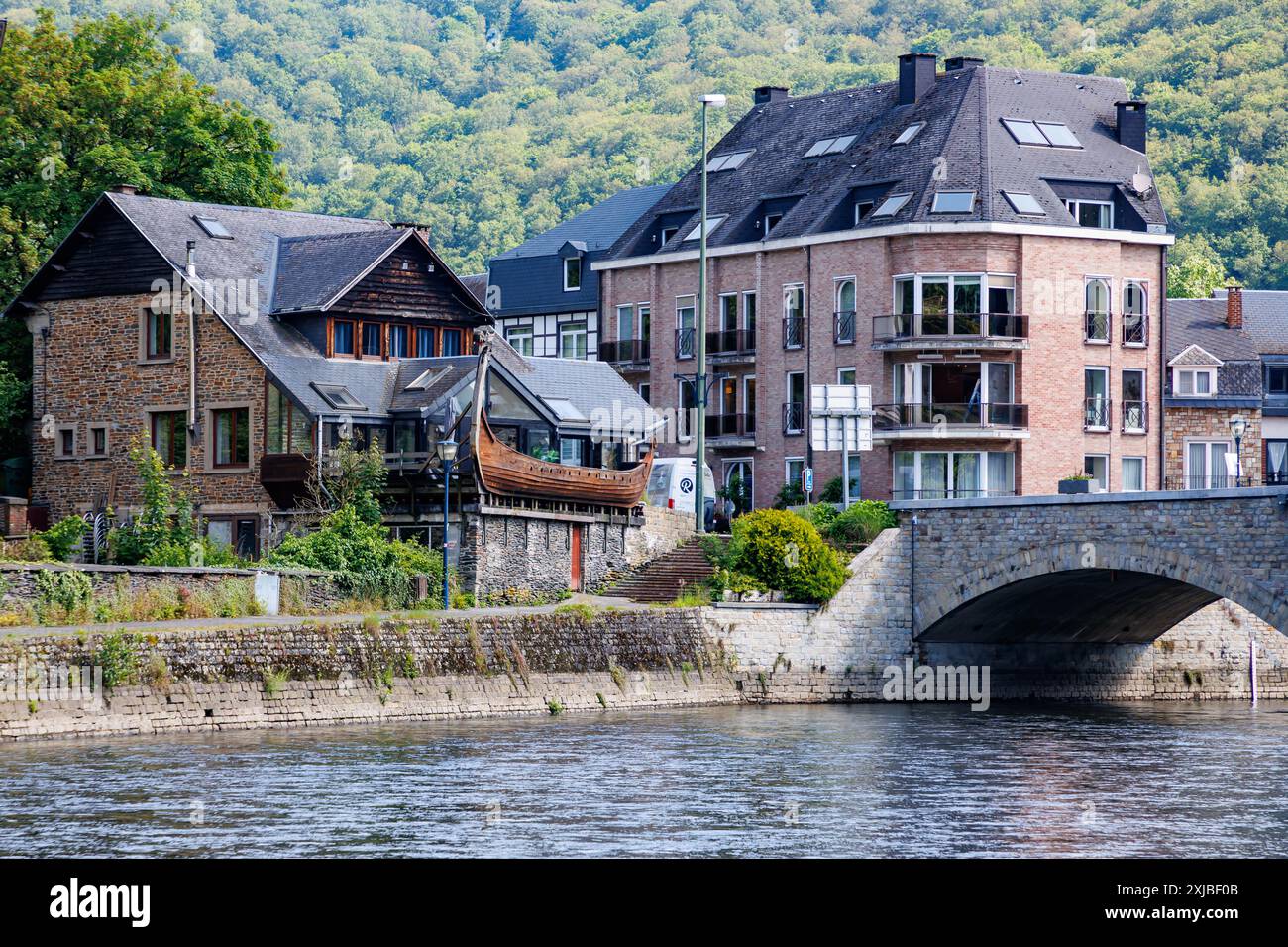 Partial view of Ourthe river, wooden Viking boat next to a building ...