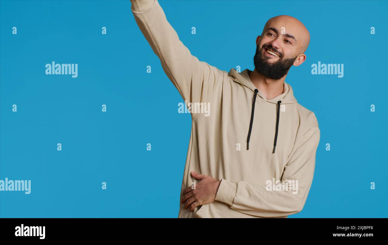 Arab man waving at a person while posing in studio, feeling happy and ...