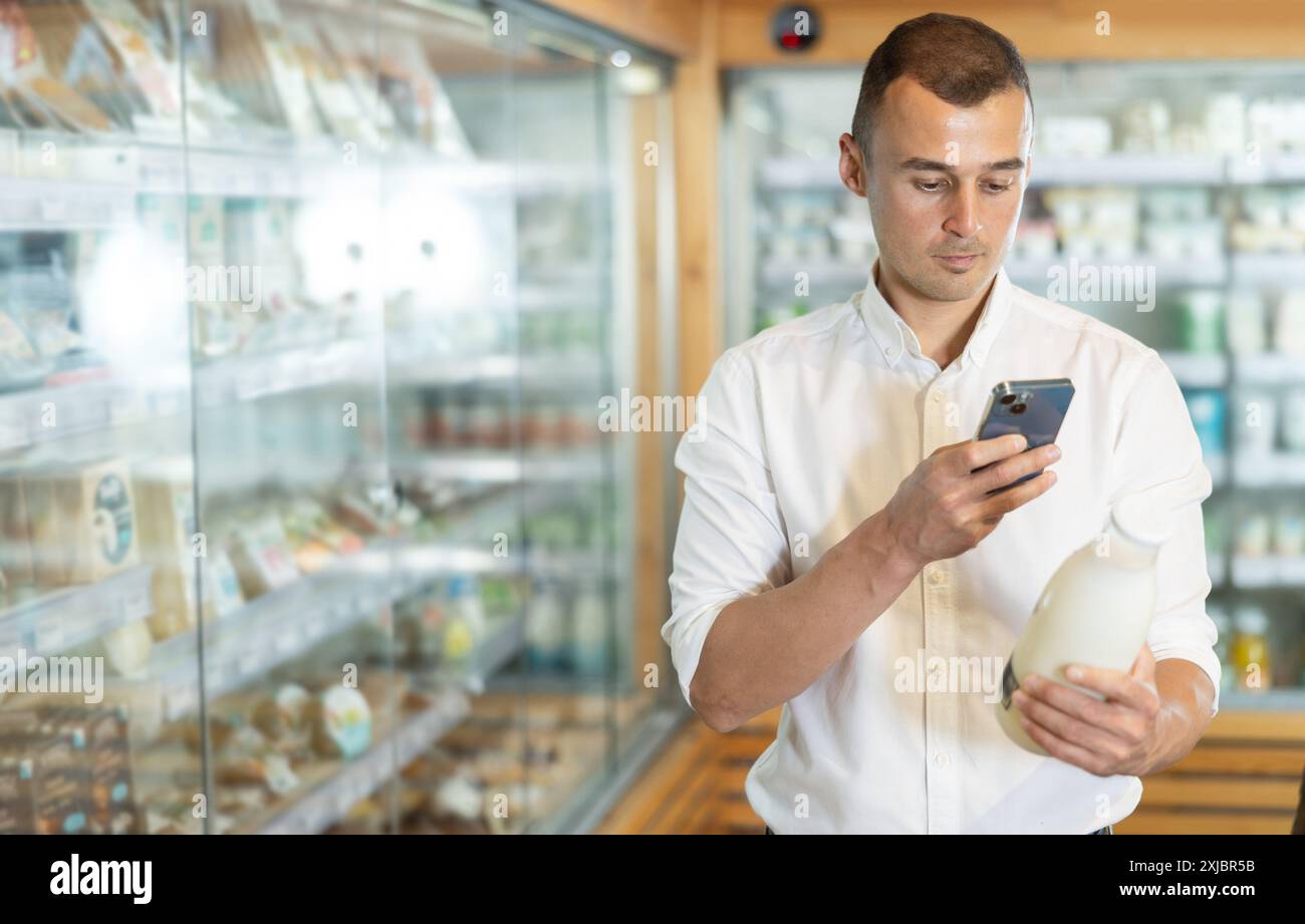 Attentive young man scanning QR code on milk bottle in large ...