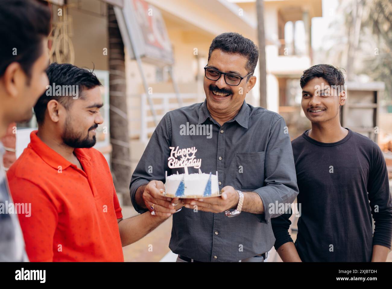 Group of four happy men. Man in shirt, glasses accepts birthday cake ...
