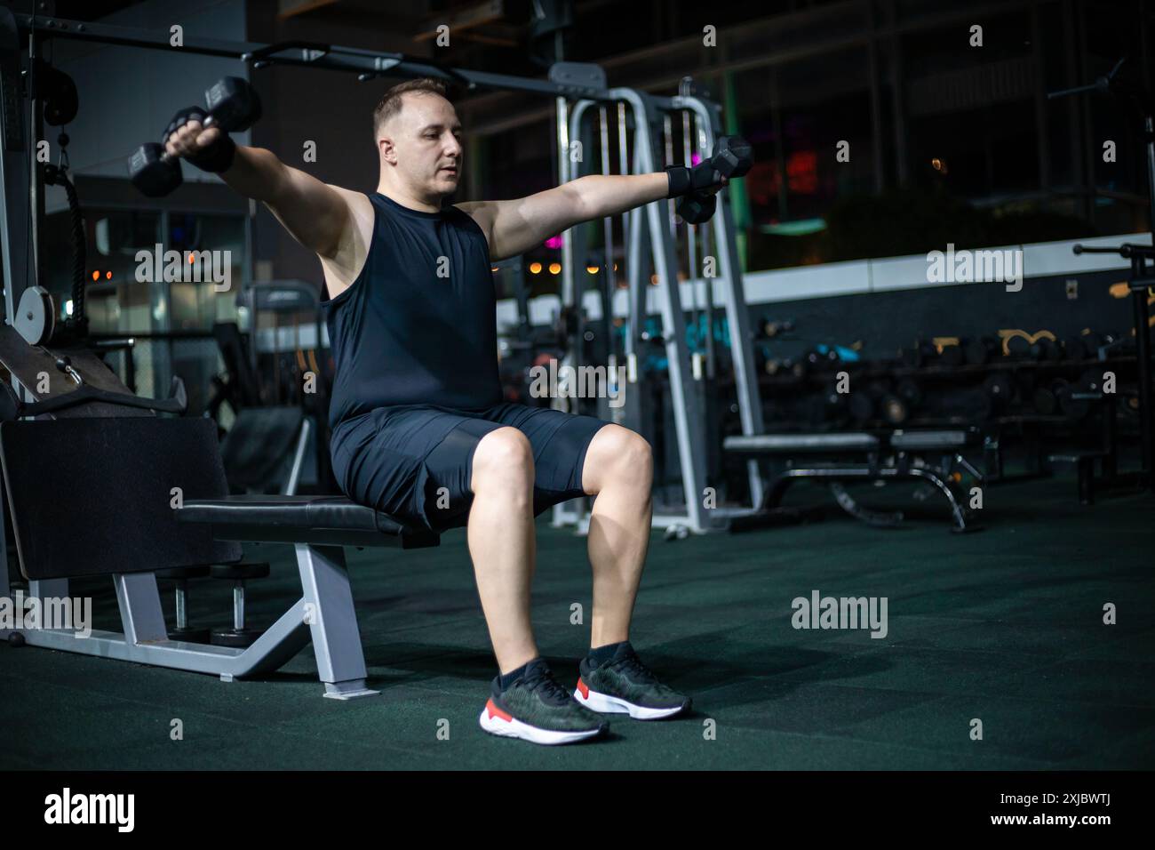 A man lifts weights while sitting on a bench in a gym Stock Photo - Alamy