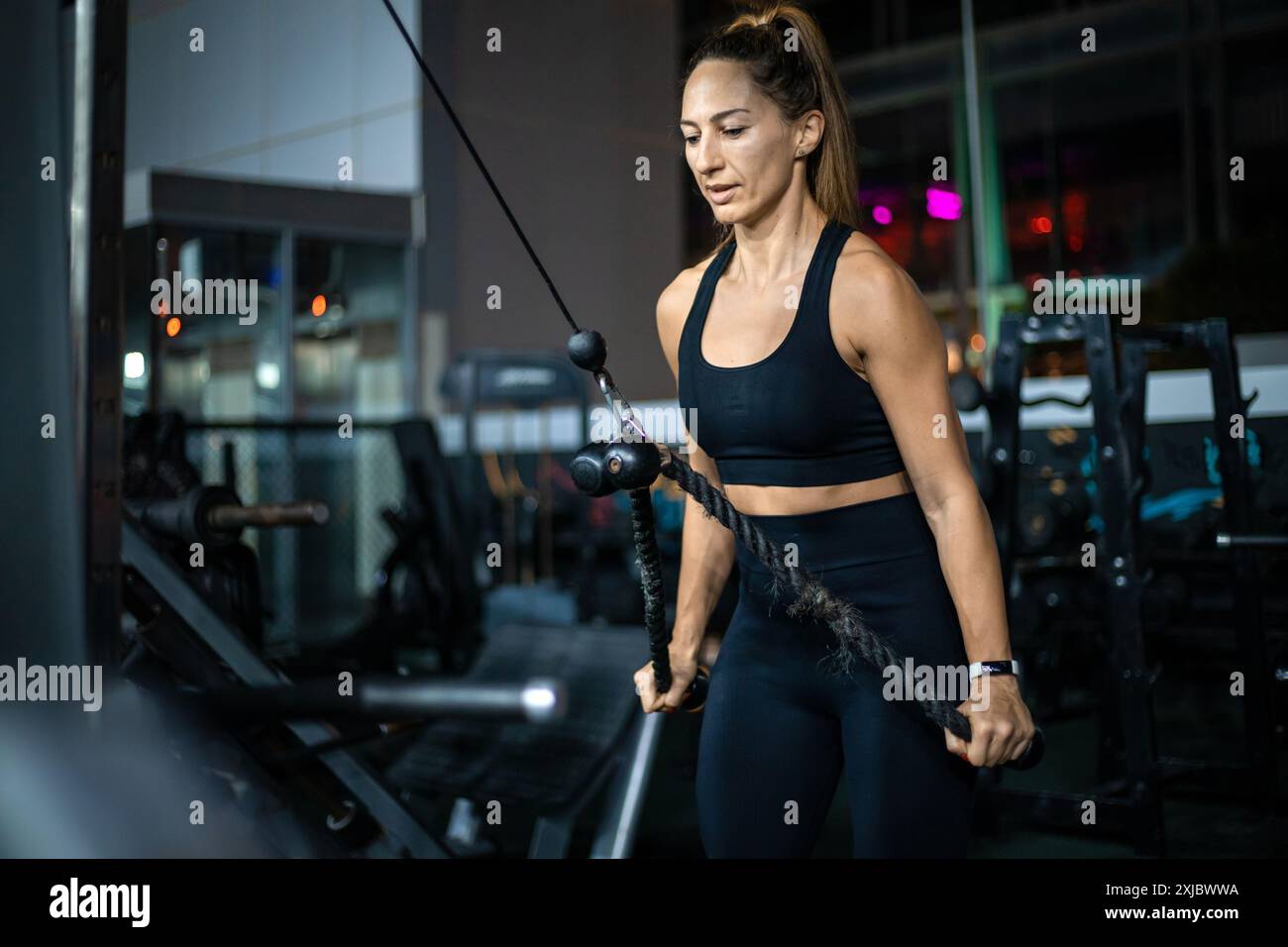 A woman in black athletic wear works out with a cable machine in a gym ...