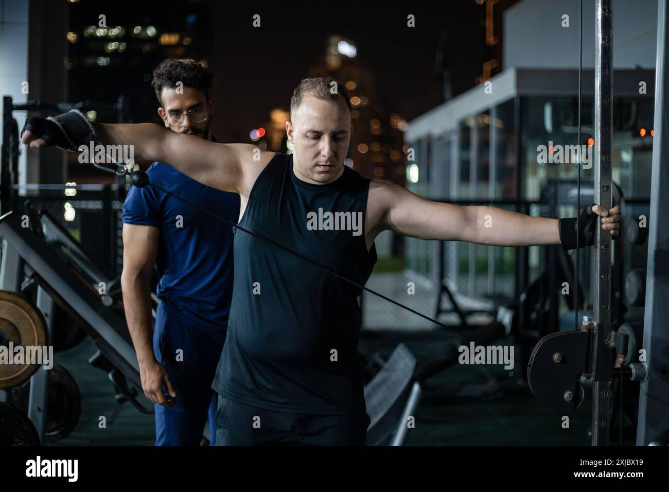 A man works out with a personal trainer in a gym, doing shoulder ...