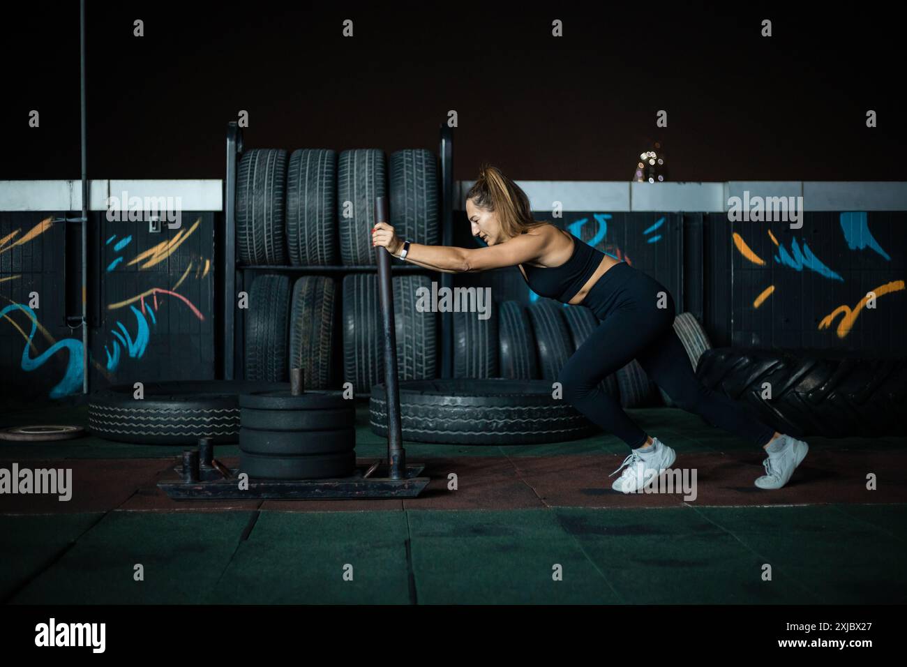 A woman in a black sports bra and leggings pushes a tire across a ...