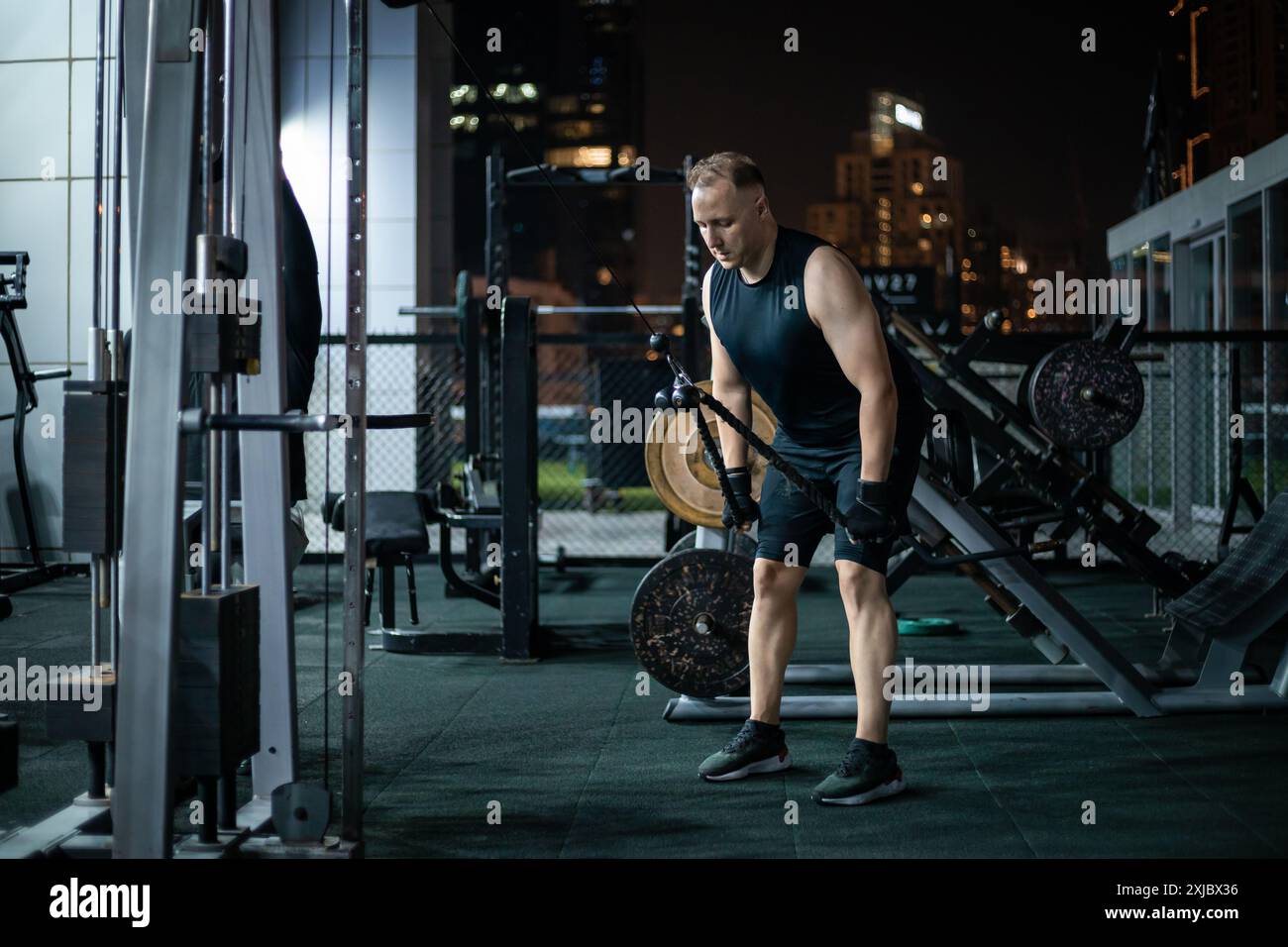 A man in black athletic wear works out on a cable machine in a gym at ...
