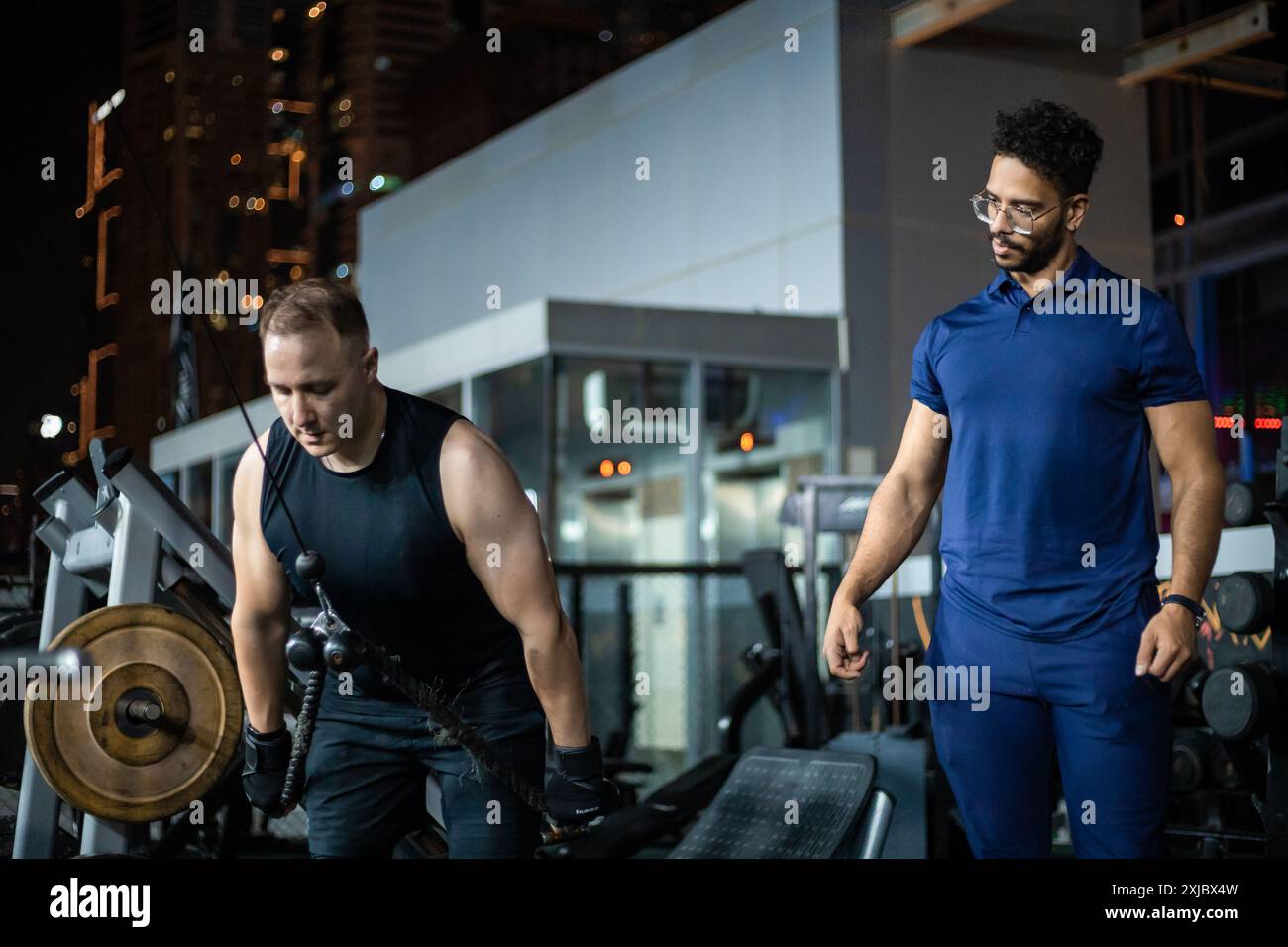 A man lifts weights on a machine in a gym with his personal trainer ...