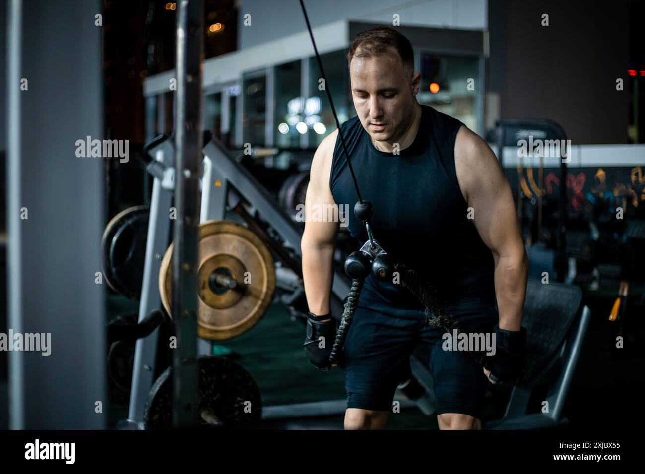 A man in a gym works out using a cable machine, pulling down on a cable ...