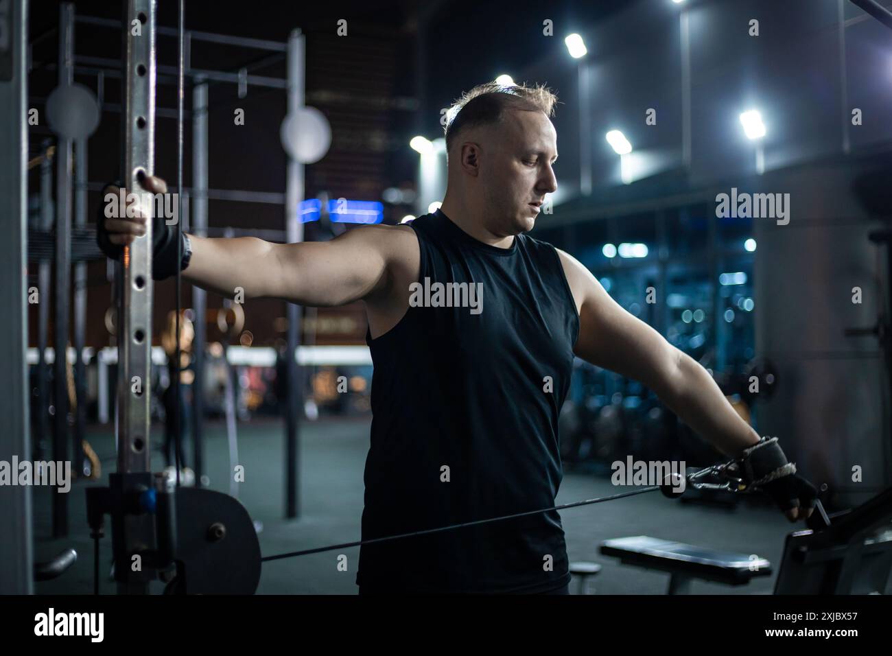 A man performs a cable fly exercise in a dimly lit gym at night Stock ...