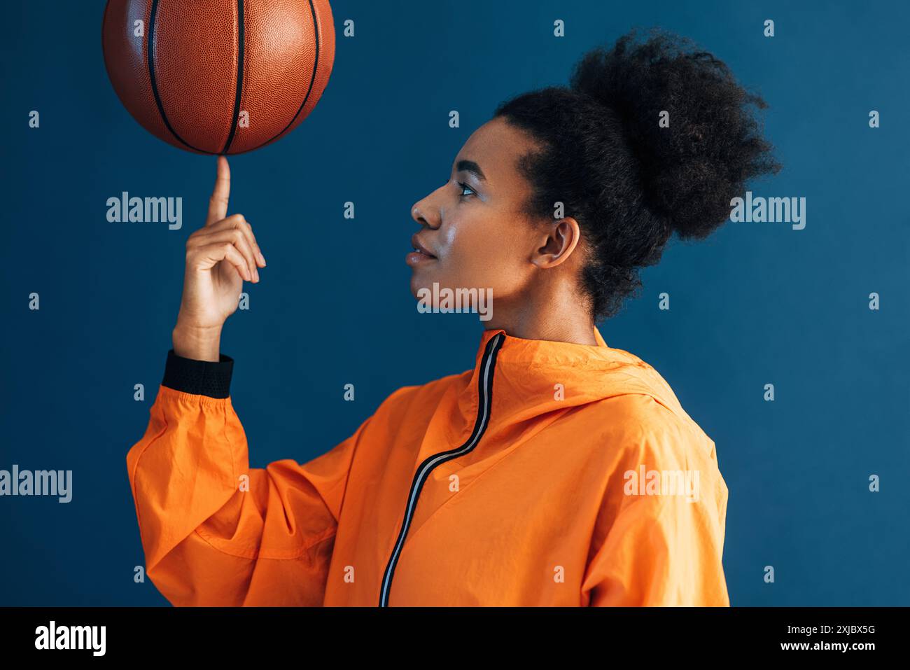 Side view of young woman with curly hair holding basketball on finger ...