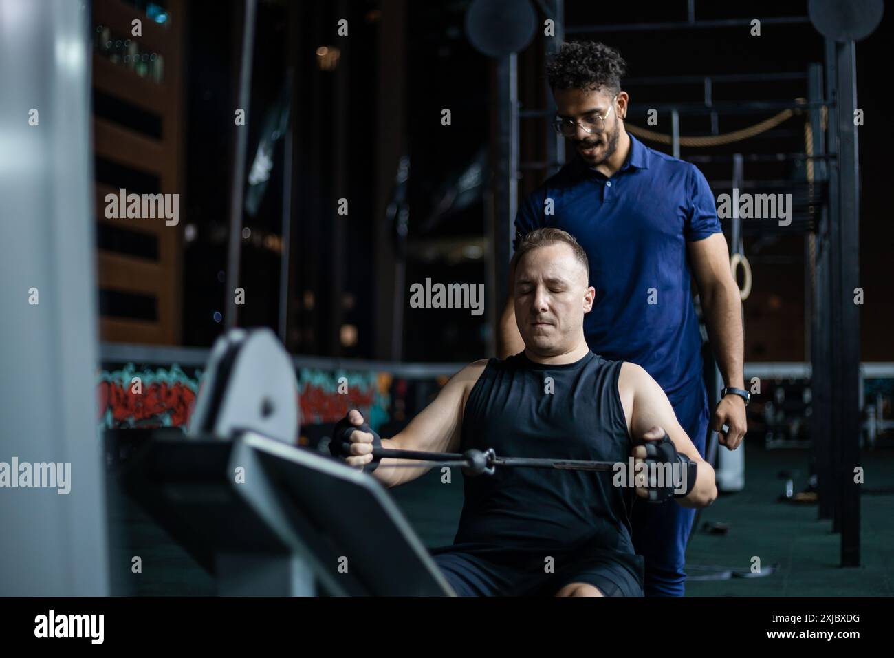 A man is doing a lat pulldown exercise on a machine in a gym at night ...