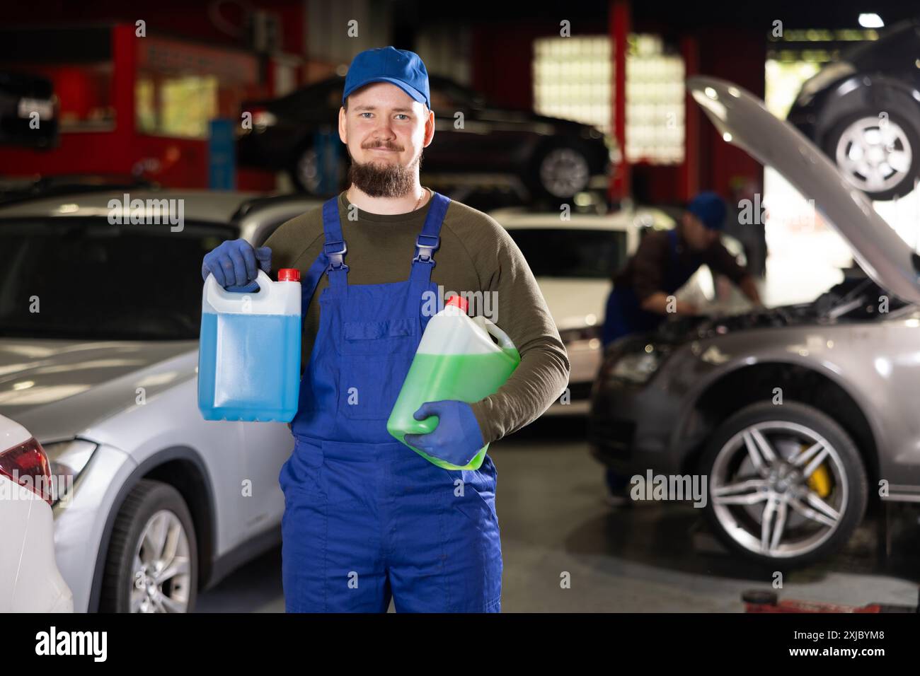 Portrait of professional auto mechanic in uniform with canisters of ...